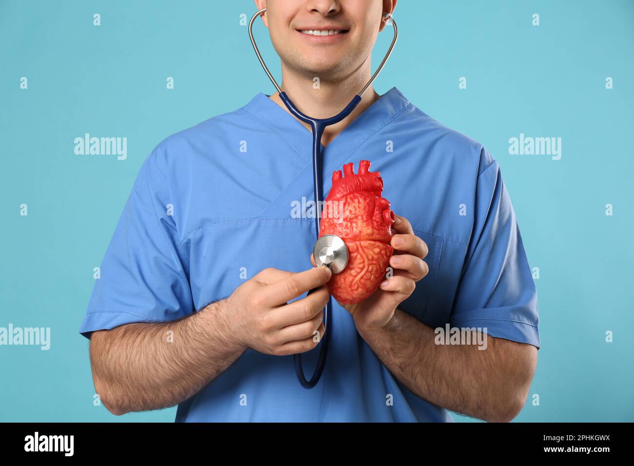 Doctor with stethoscope and model of heart on light blue background ...