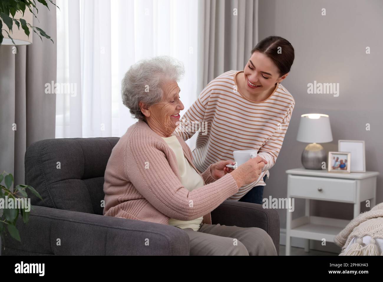 Young caregiver giving tea to senior woman in room. Home care service ...