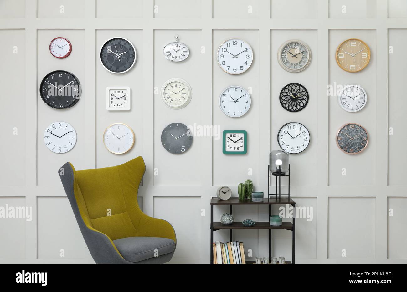 Armchair, console table and many different clocks hanging on white wall ...