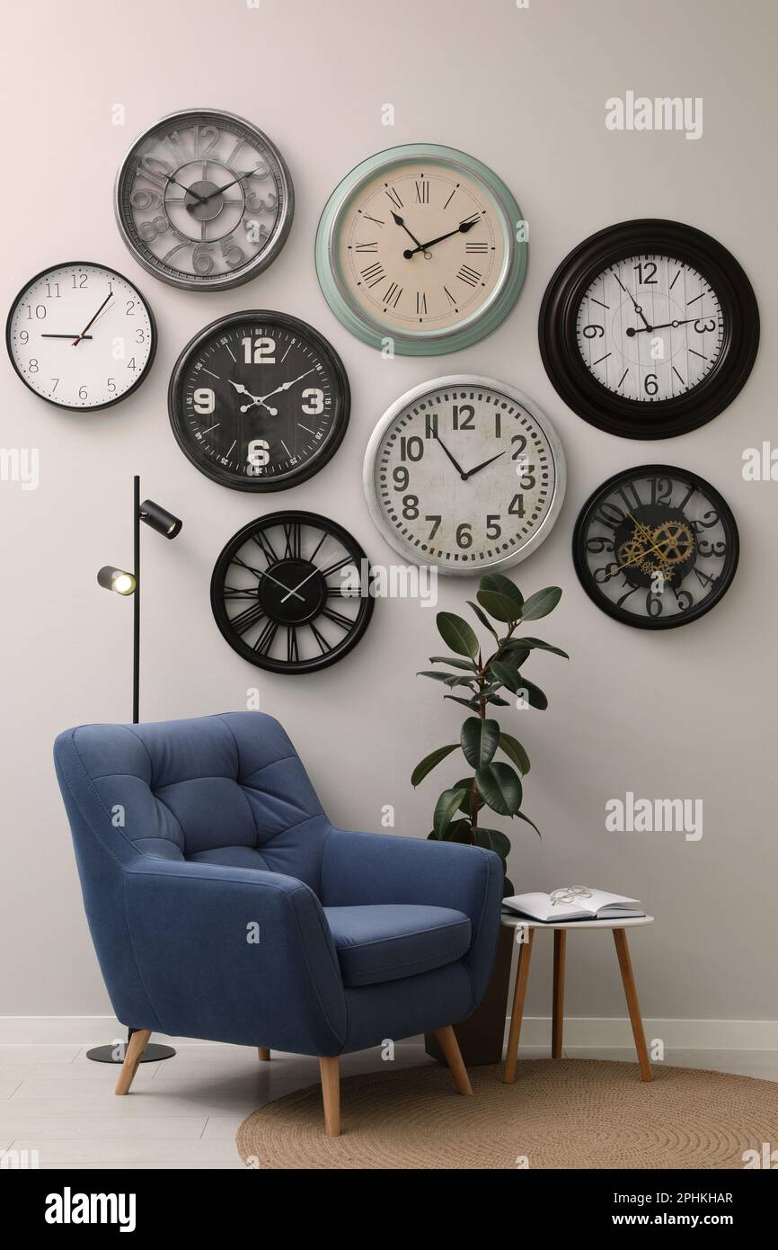 Armchair, table and many different clocks hanging on white wall in room ...