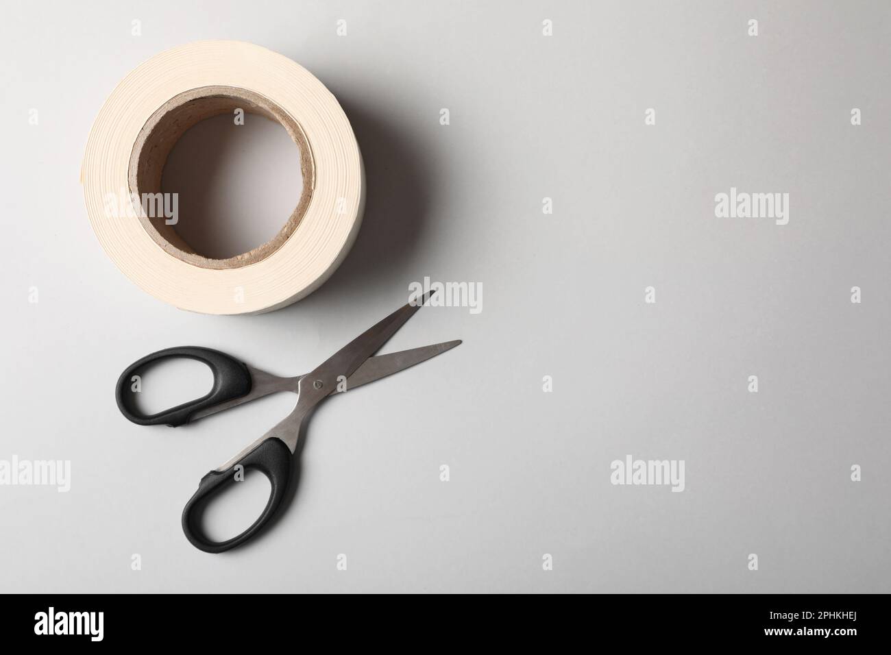 Roll of adhesive tape and scissors on light background, top view. Space ...