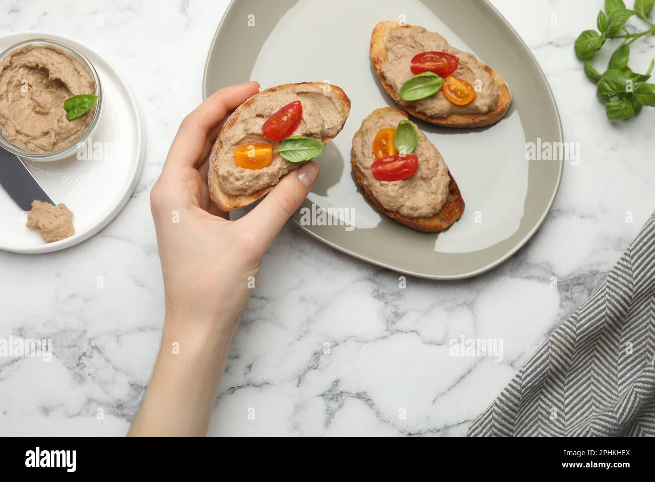 Woman taking slice of bread with delicious pate at white marble table ...