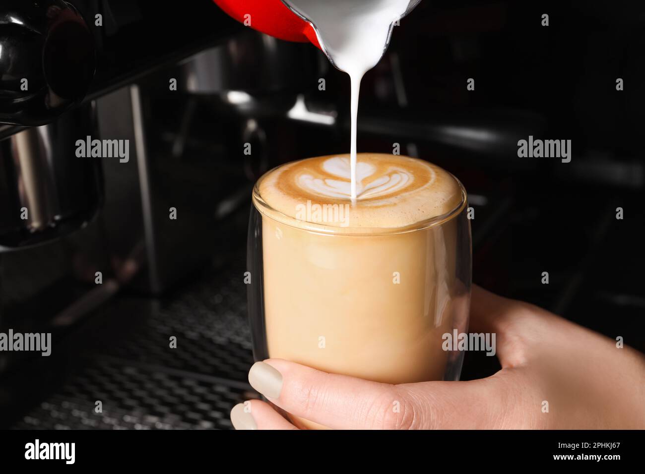 Barista pouring steamed milk from pitcher into glass cup of fresh ...