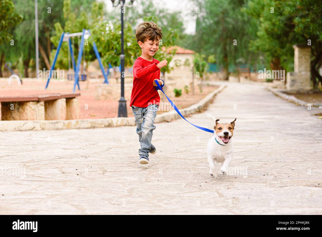 Happy smiling small boy playing and running with his pet dog in park ...