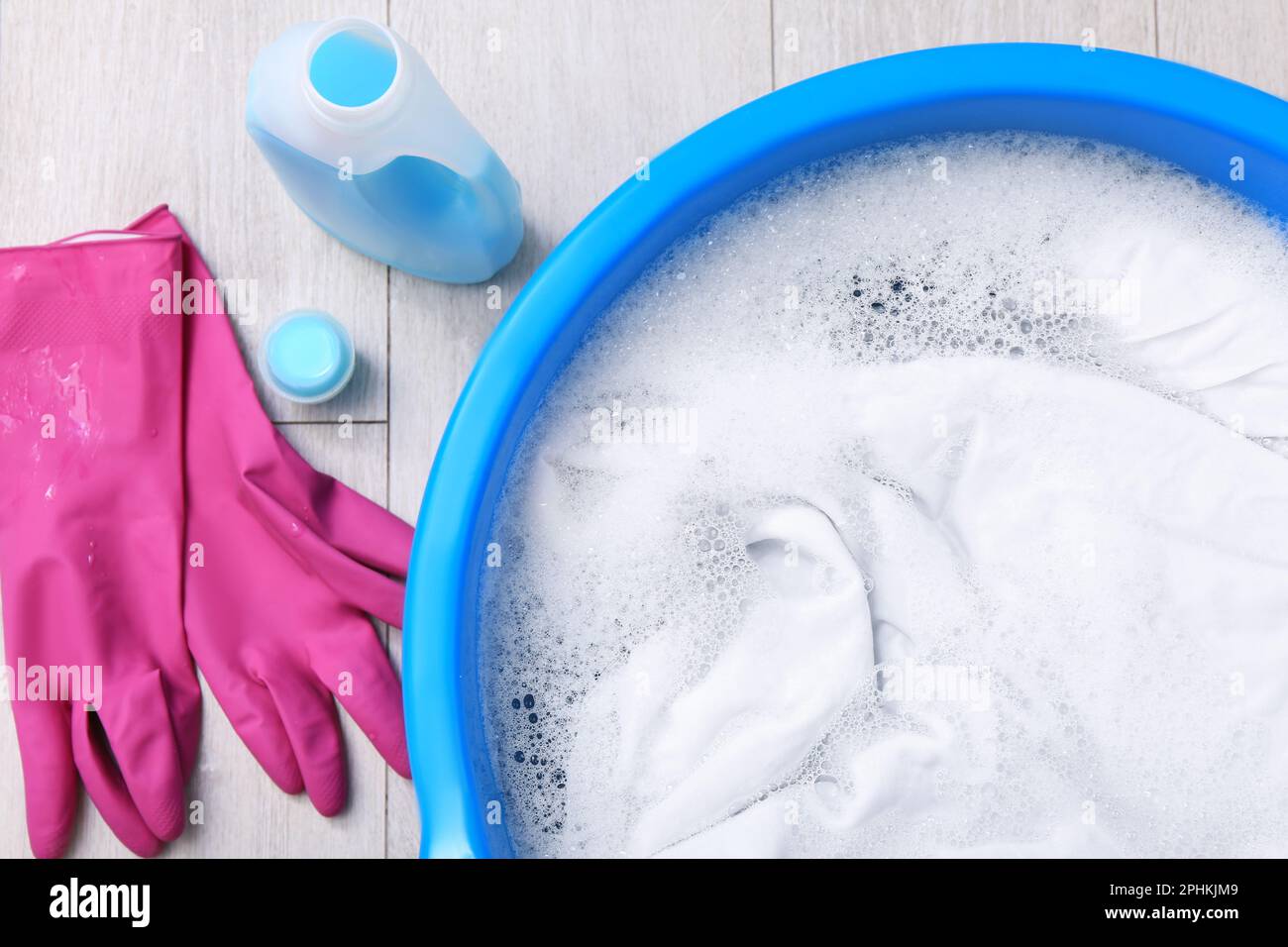 Basin with white garment near detergent and gloves on floor, flat lay ...
