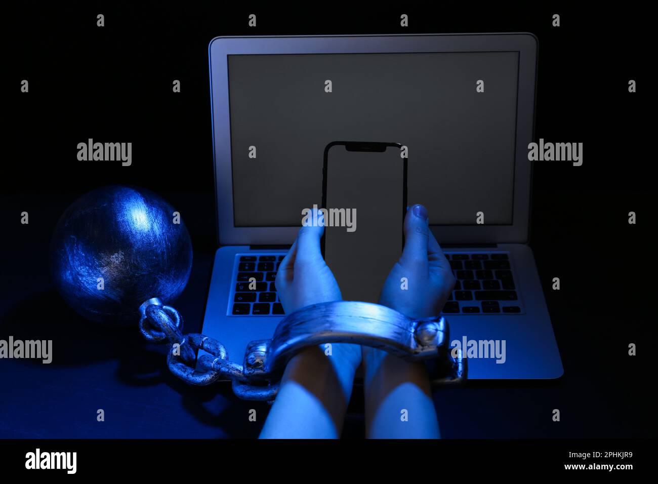 Woman shackled with ball and chain holding smartphone near laptop on ...