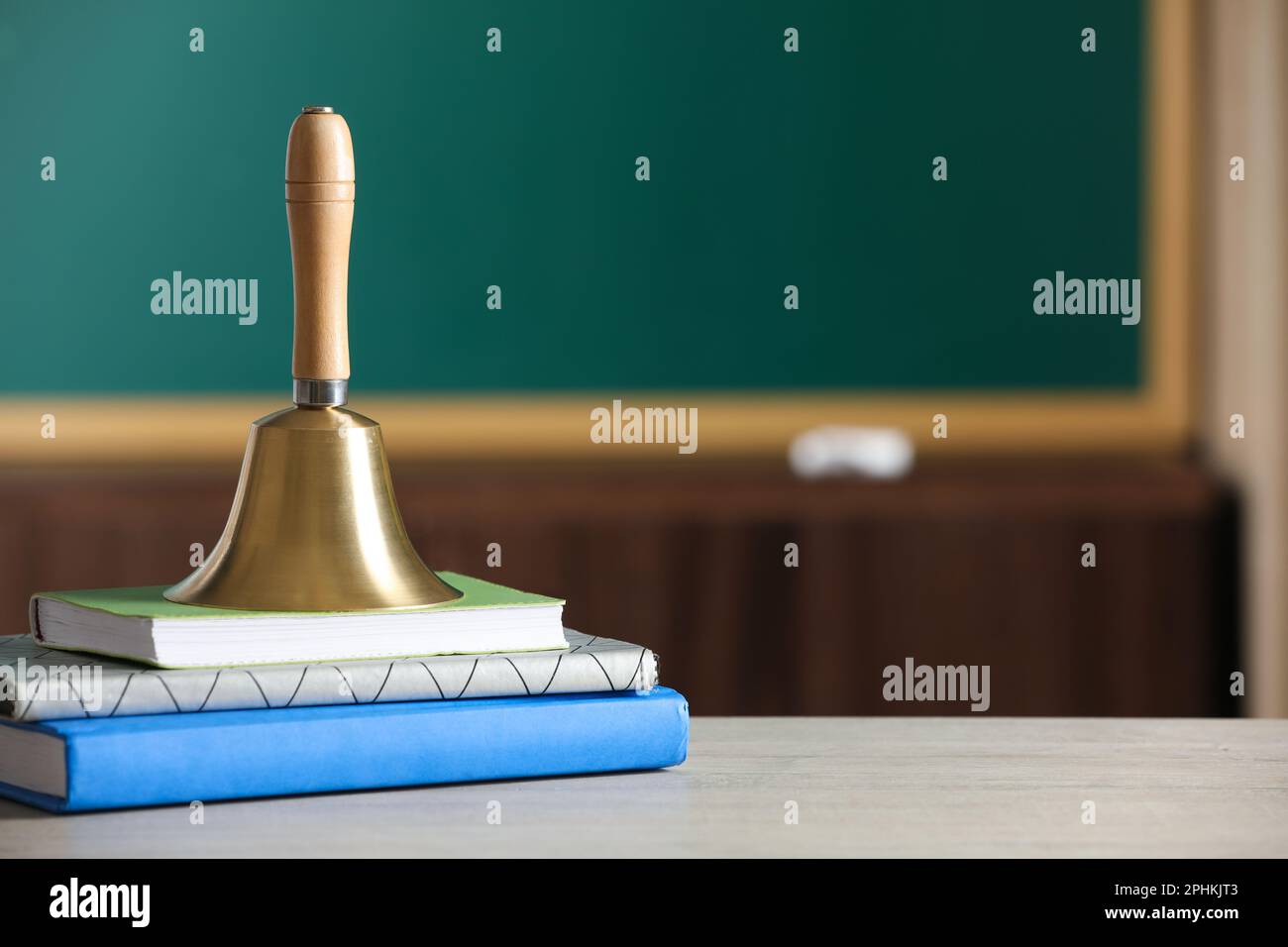 Golden school bell and books on wooden table in classroom, space for ...