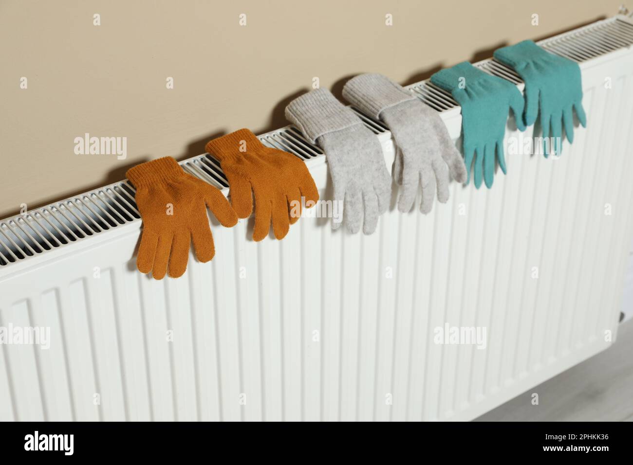 Modern radiator with knitted gloves near beige wall indoors Stock Photo ...