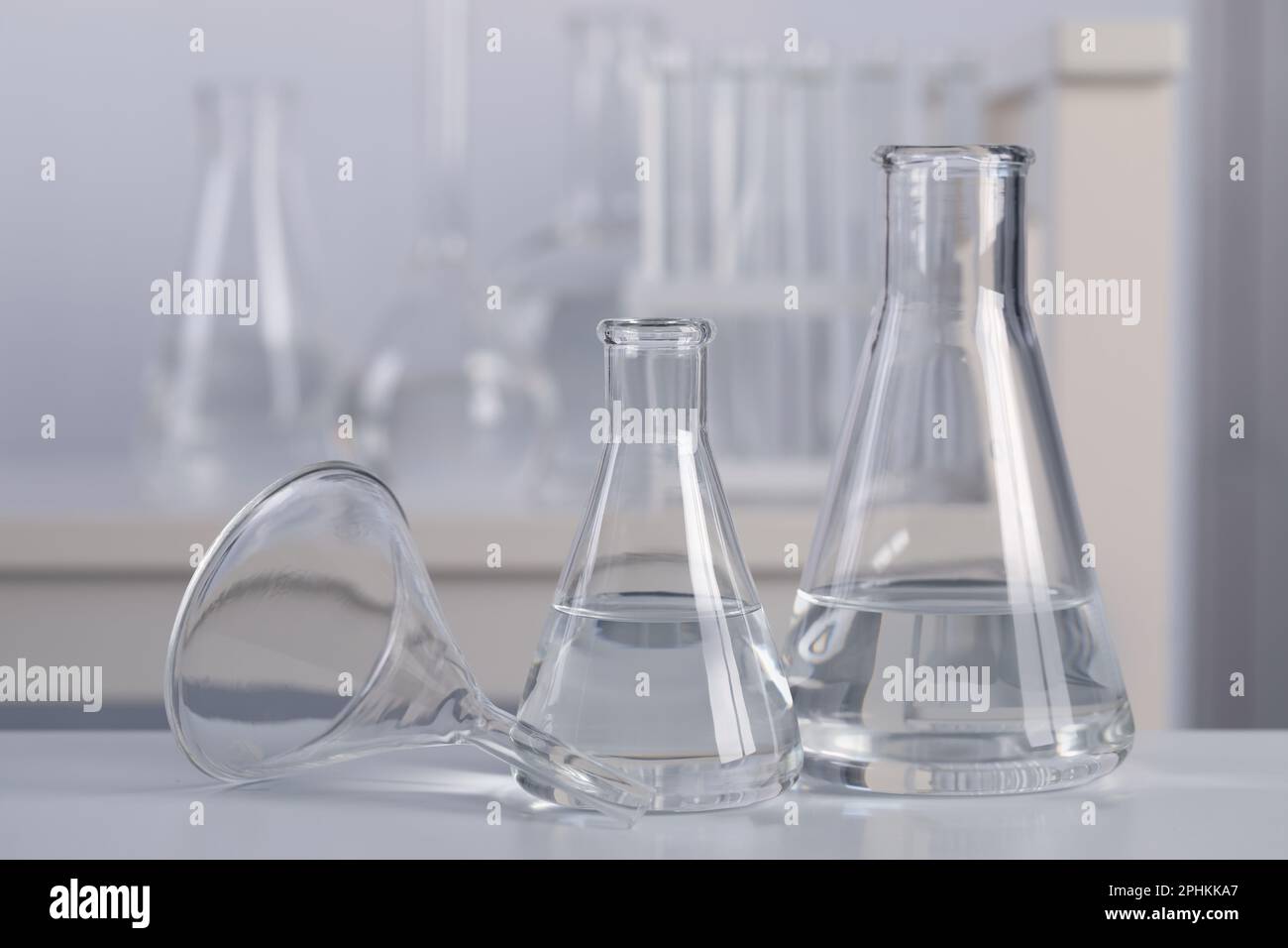 Conical flasks with transparent liquid and funnel on table in ...