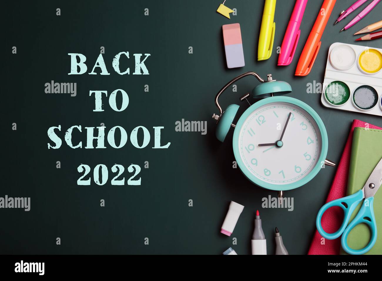 Back to school 2022. Flat lay composition with alarm clock and different stationery on green ...