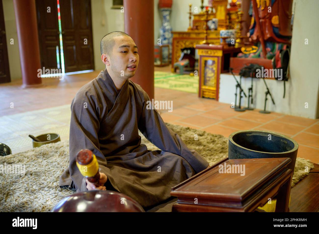 Young Asian monk in black outfit sitting in temple and hitting bowl ...