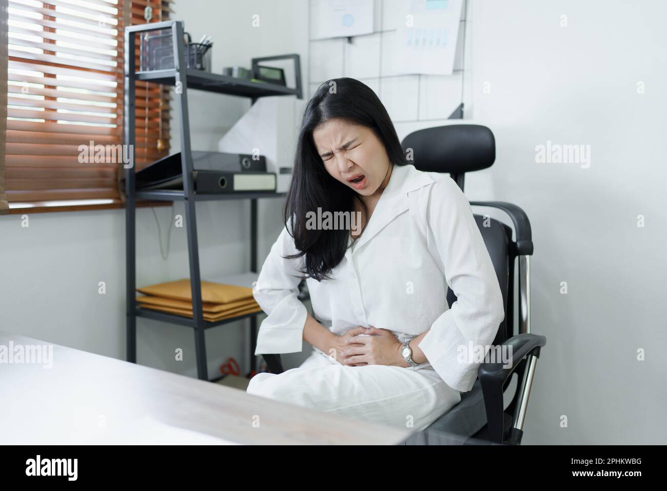 Portrait of a young Asian female representative showing acute abdominal ...