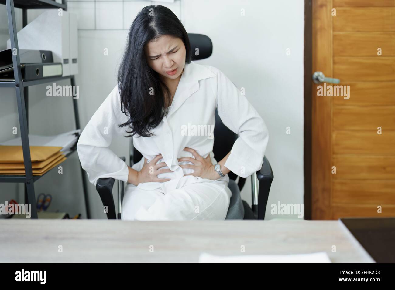 Portrait of a young Asian female representative showing acute abdominal ...