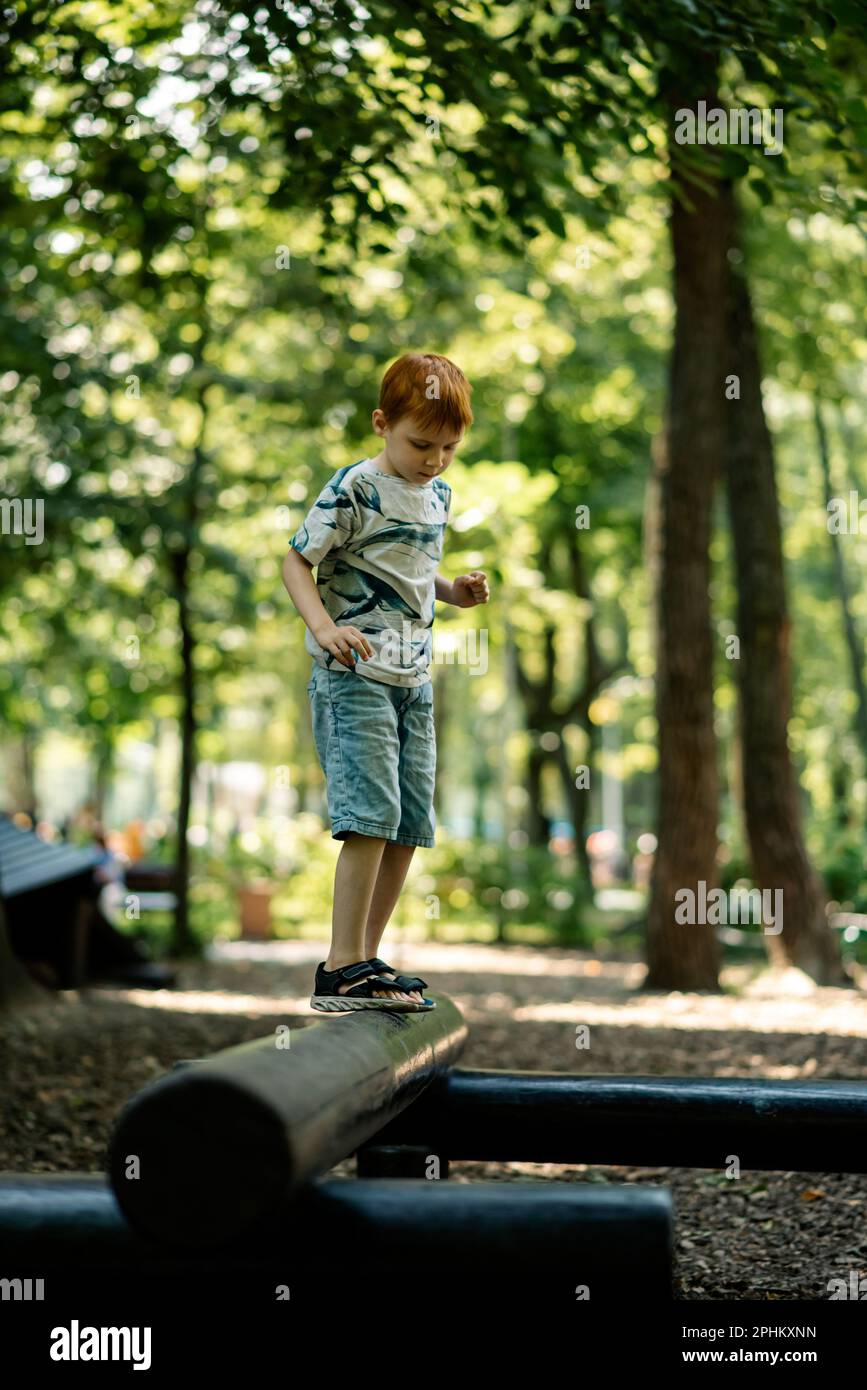 A young boy walks on a log at the playground. Active summer vacation ...