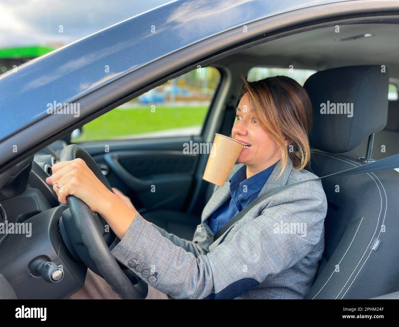 side view of businesswoman driving a car in city with traffic holding ...