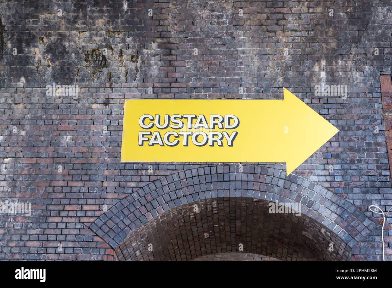 Yellow sign on wall of railway arch pointing to entrance to the Custard ...