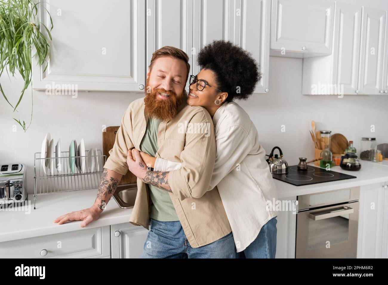 Cheerful african american woman hugging tattooed boyfriend in kitchen ...