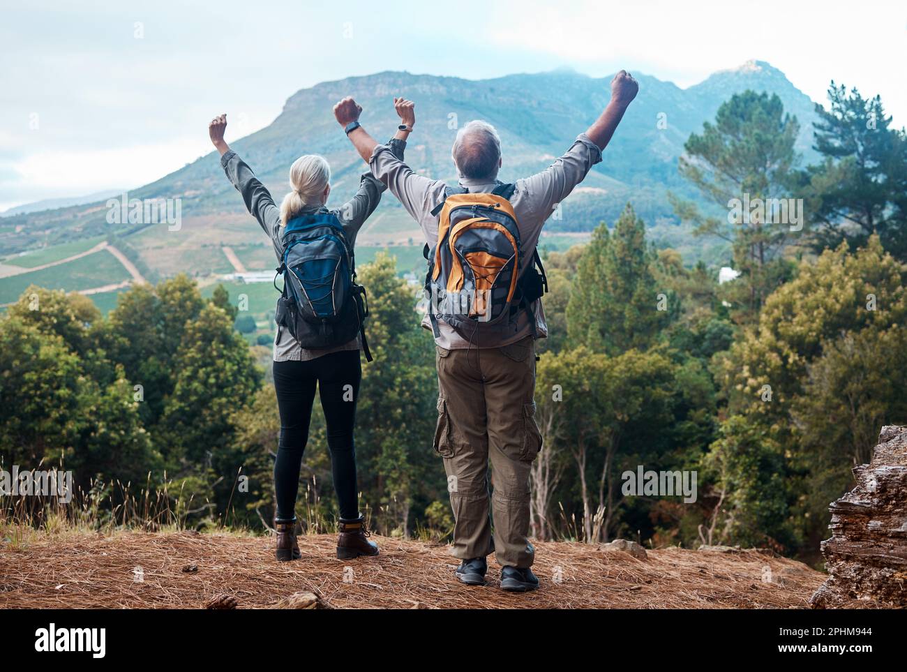 Hiking, mature couple and arms raised on cliff from back on nature walk ...