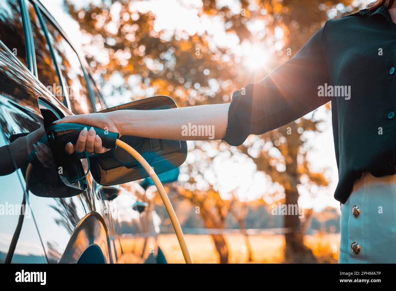 Female hand putting a cable charger in an electric car illuminated by ...