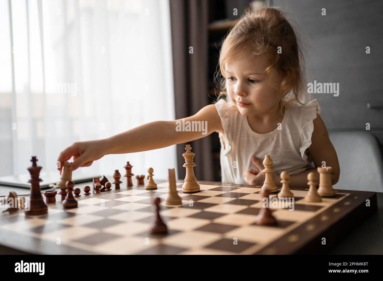 Little girl playing chess at the table in home kitchen. The concept ...