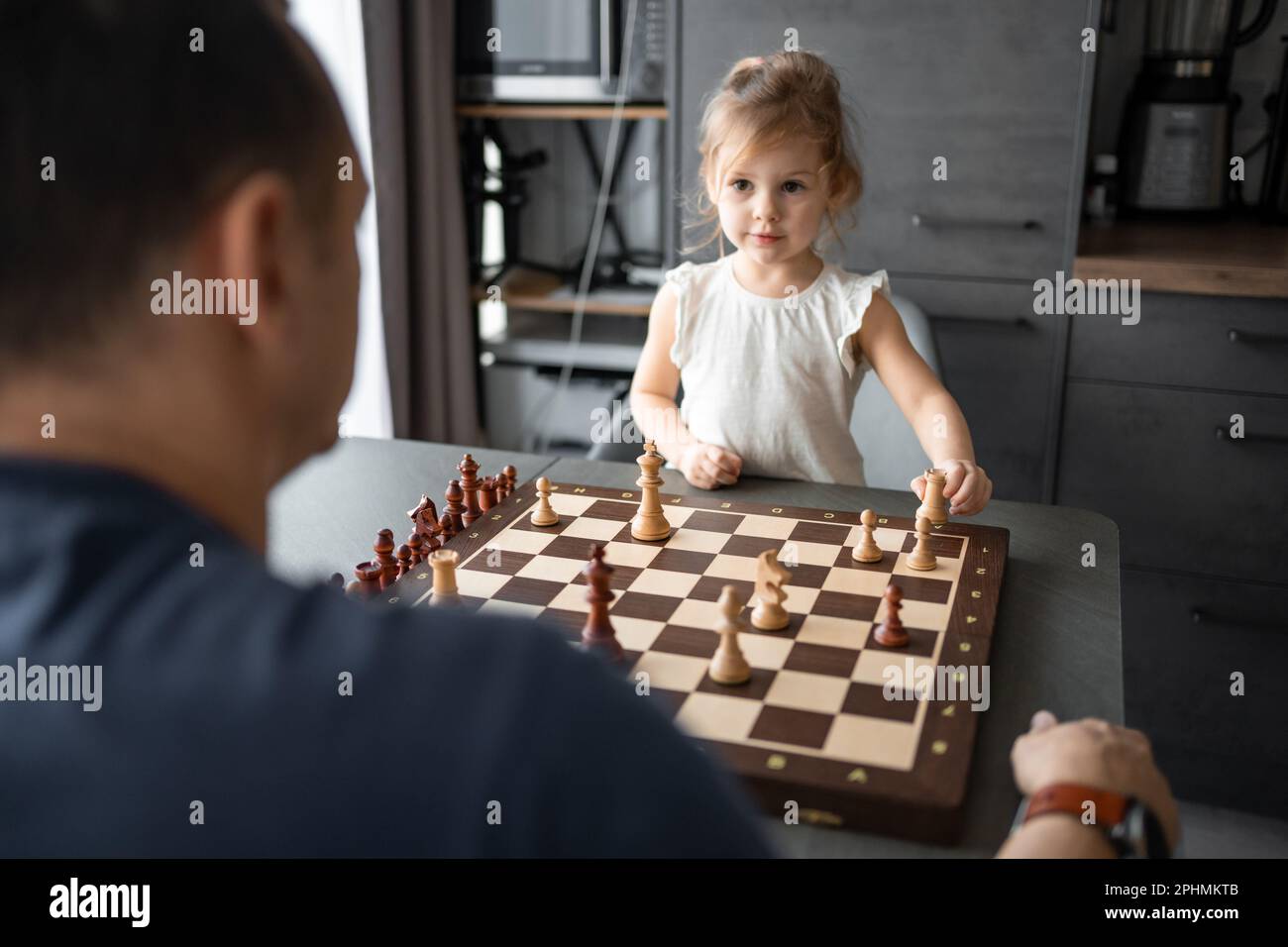 Father teaching his little daughter to play chess at the table in home ...