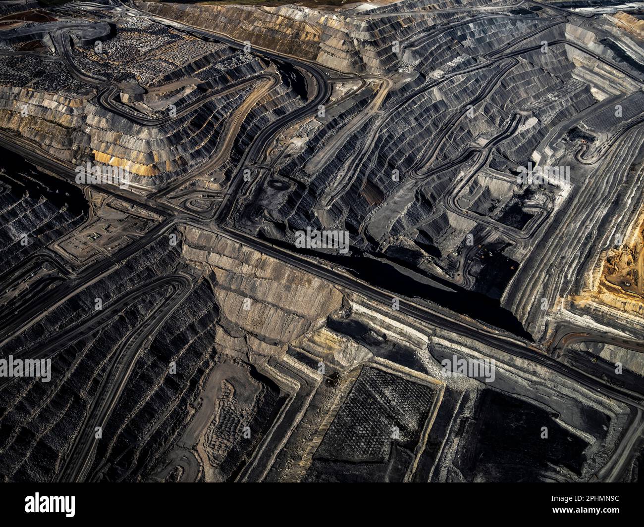 A vast open-pit excavation site filled with coal, with two smaller ...