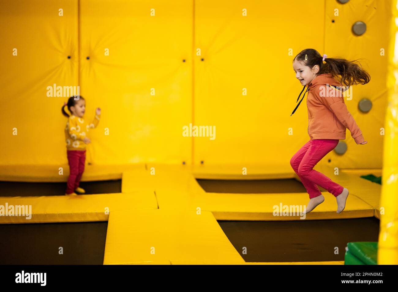 Siblings jumping on trampoline at yellow playground park. Sisters in ...