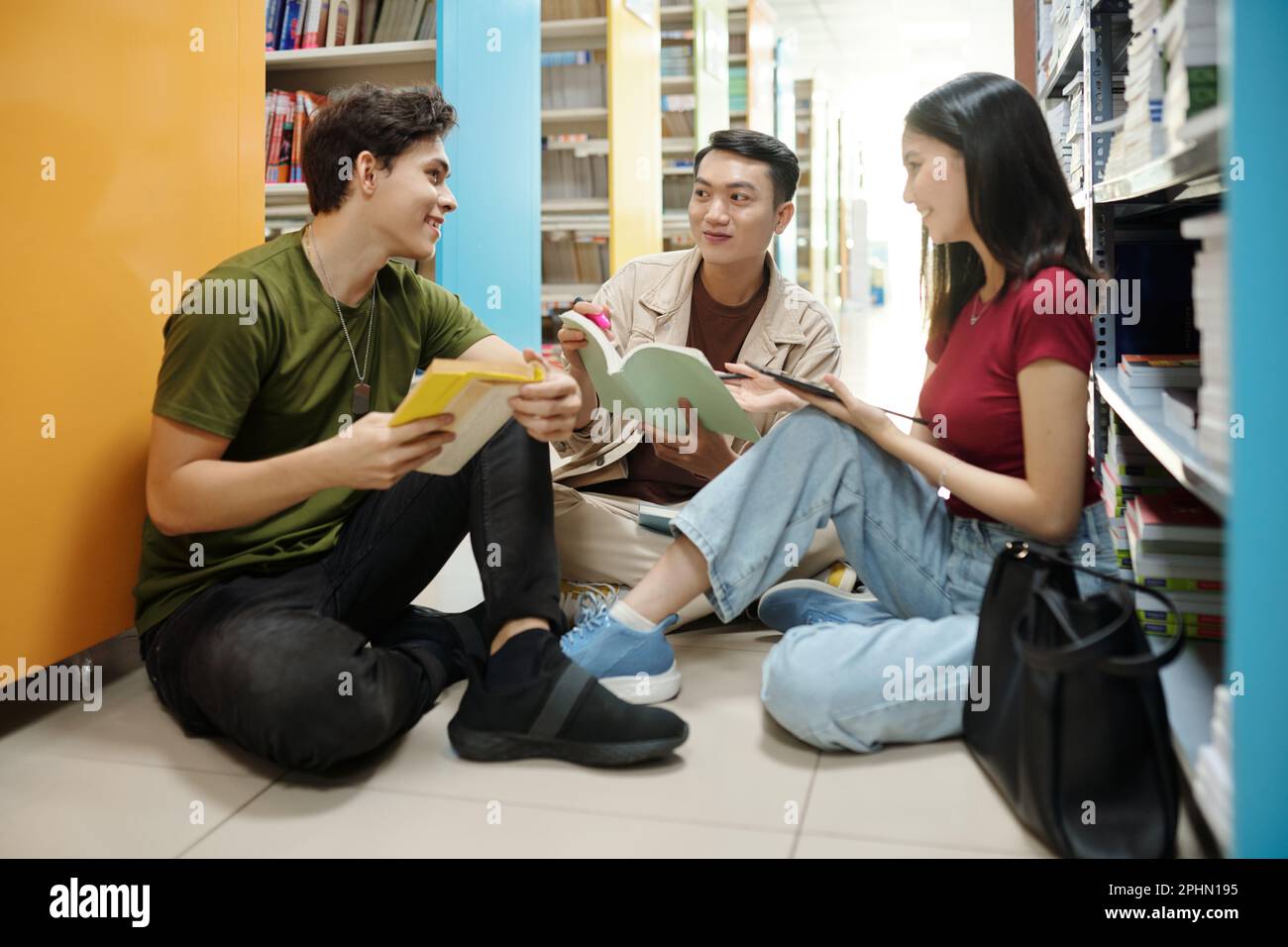 Group of happy students sitting on library floor and discussing school ...