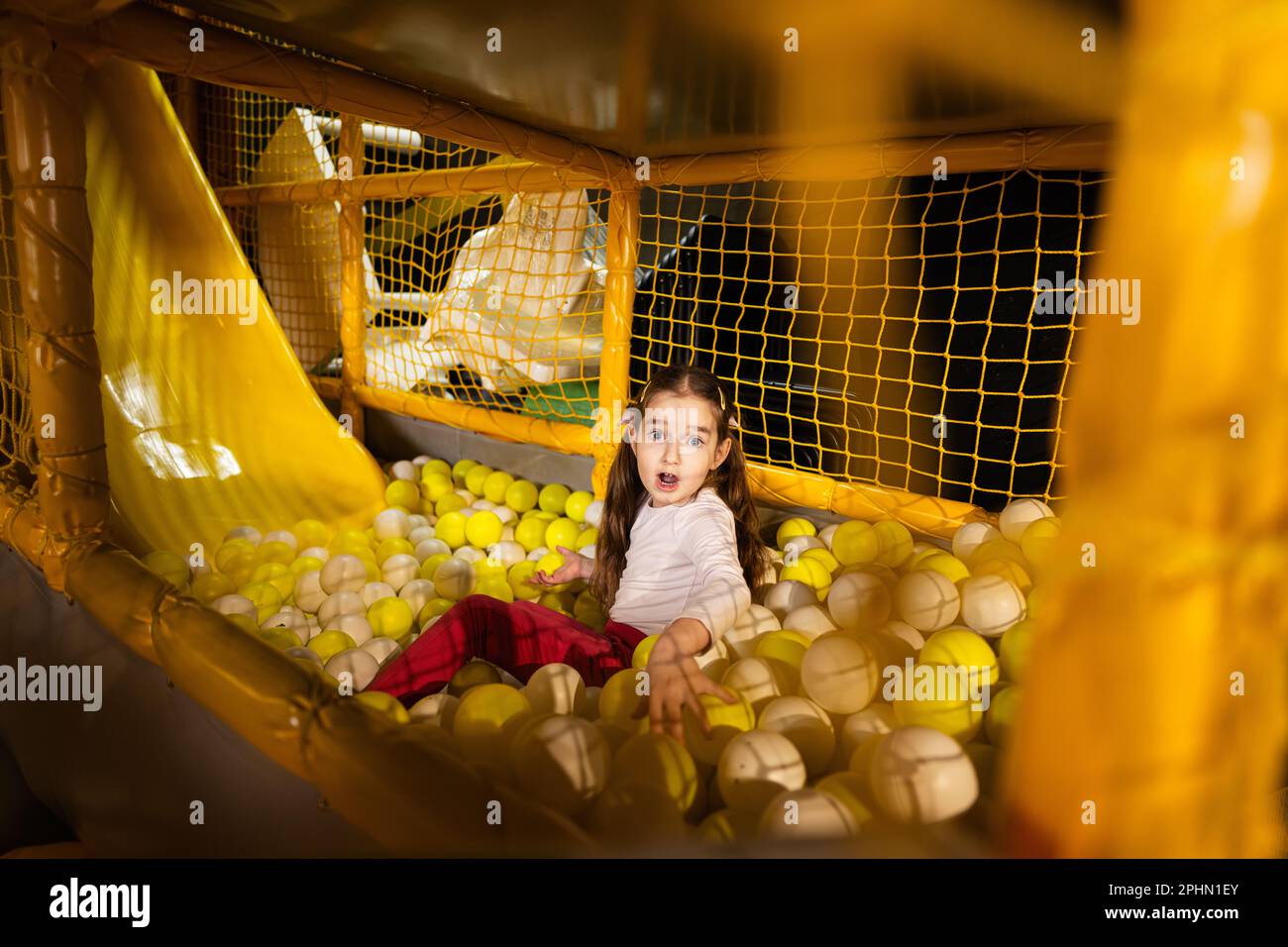 Little girl play with colored balls at yellow playground park in active ...