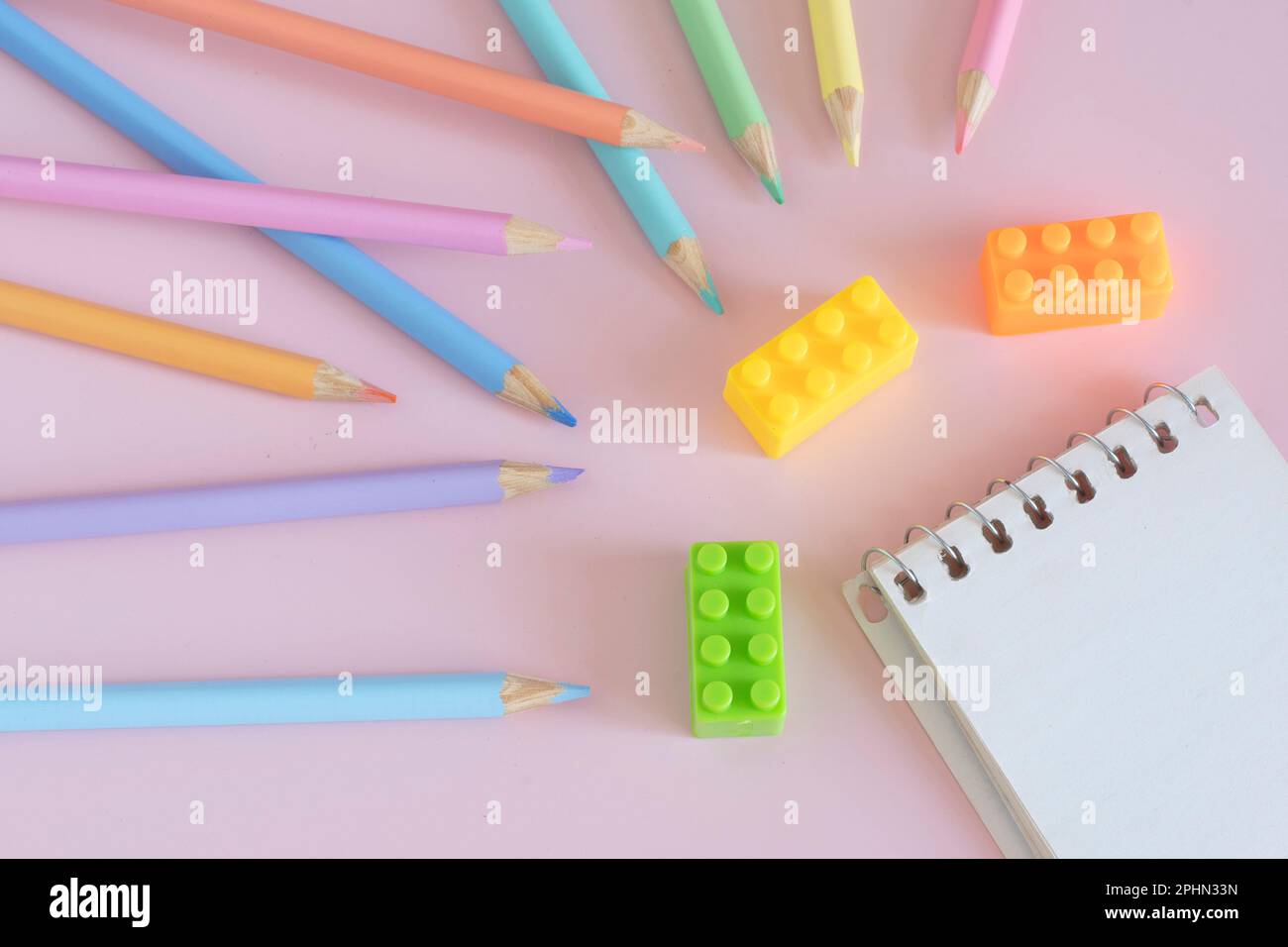 Pastel colored pencils with a notepad, top view on pink background ...
