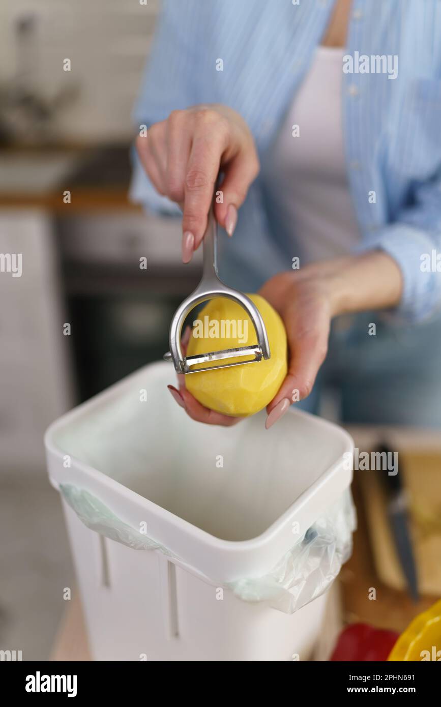Female hands peeling off potato and throwing peels in a compost bin for ...