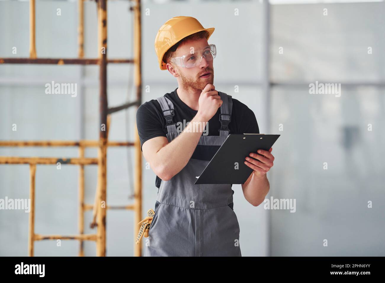Young engineer in grey uniform with notepad works indoors in modern big ...