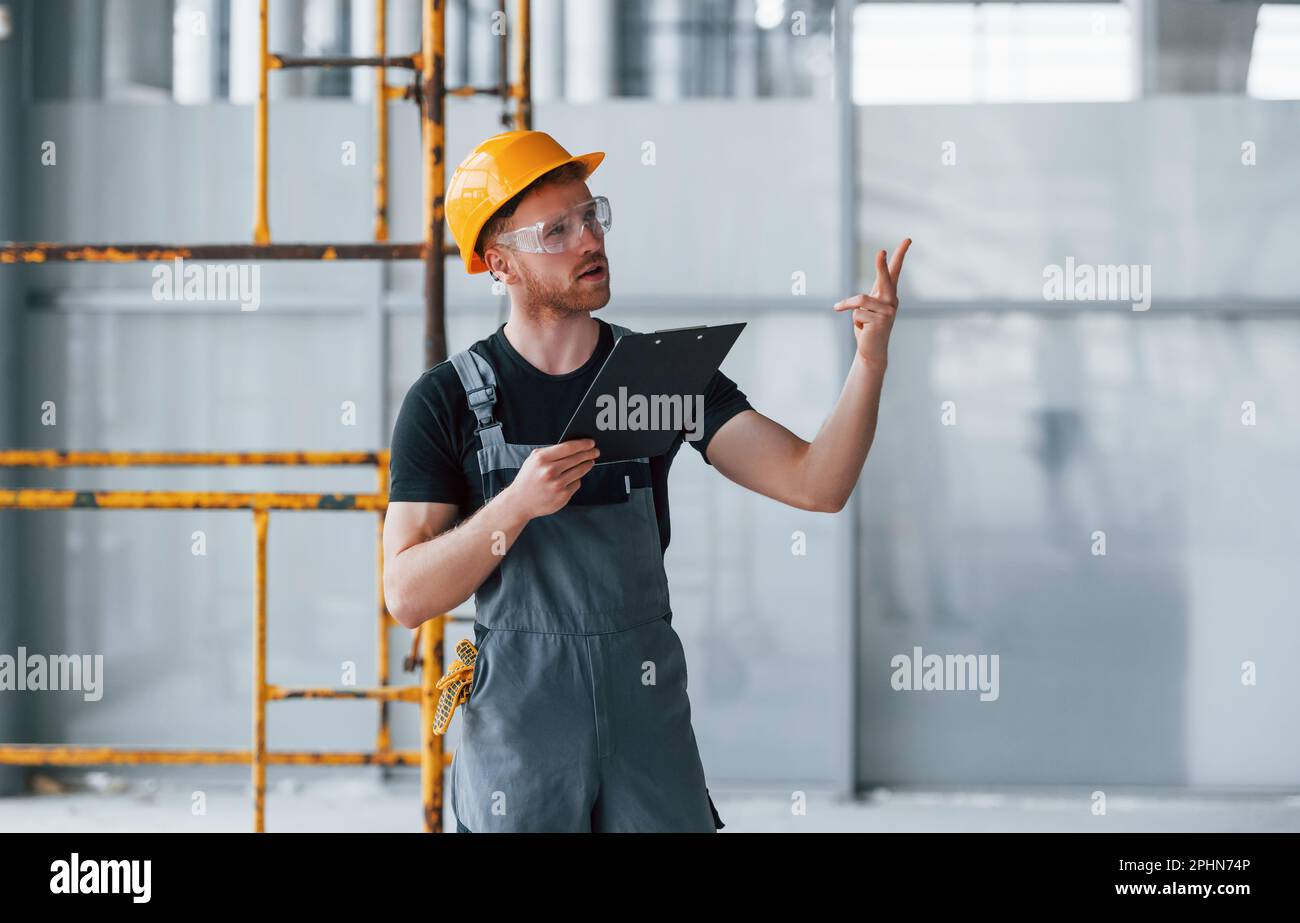 Young engineer in grey uniform with notepad works indoors in modern big ...