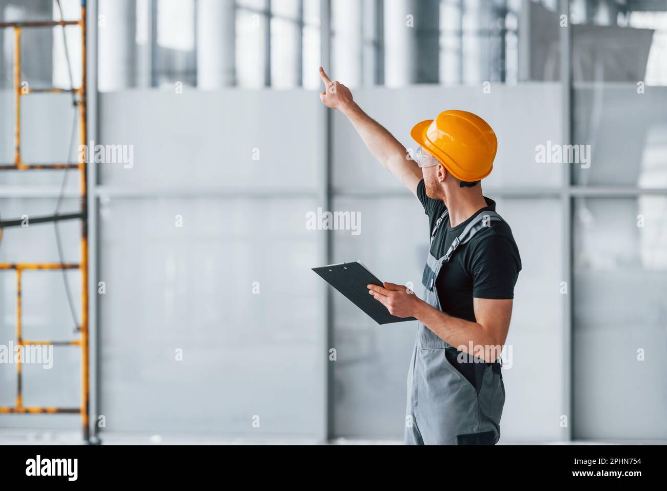 Young engineer in grey uniform with notepad works indoors in modern big ...
