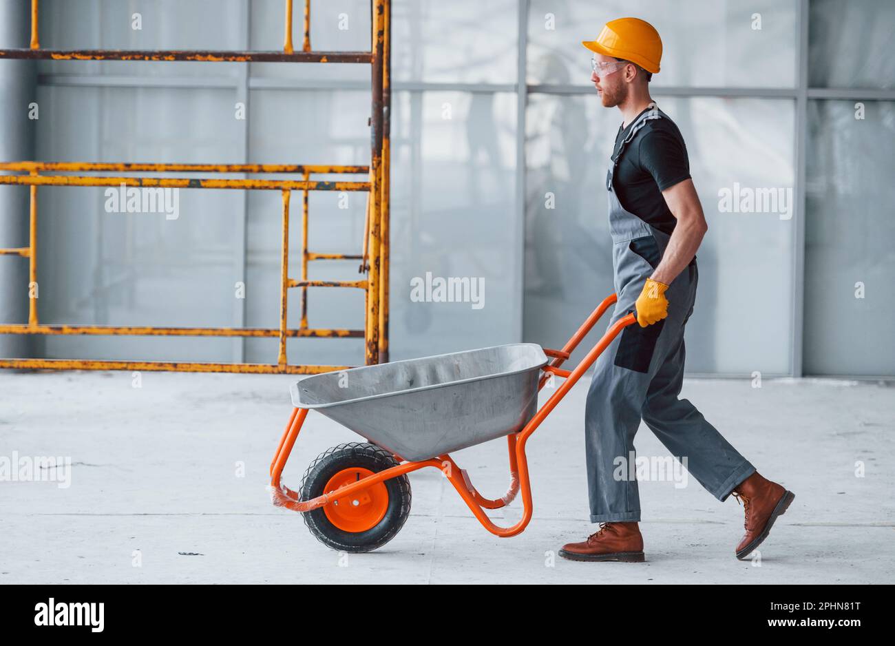 Walks with wheelbarrows. Man in grey uniform works indoors in modern ...