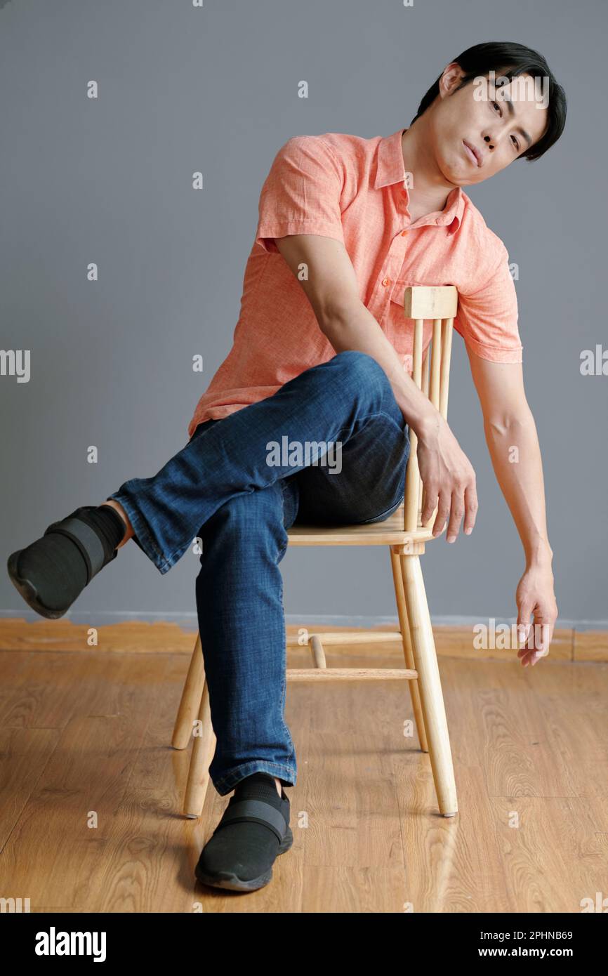 Young man in jeans and salmon shirt resting on chair Stock Photo - Alamy