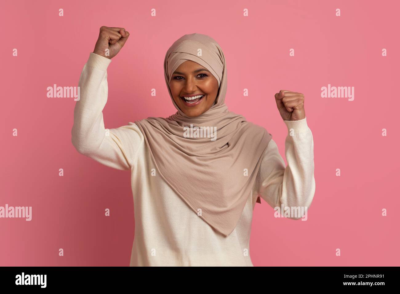 Portrait of joyful arabic woman in hijab celebrating success over poink ...