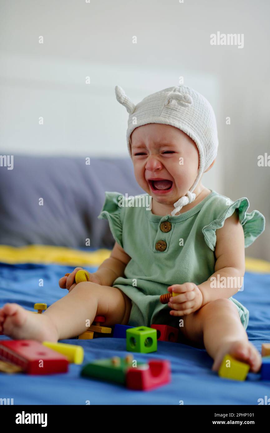 Tired little kid sitting on bed with wooden blocks around and crying ...