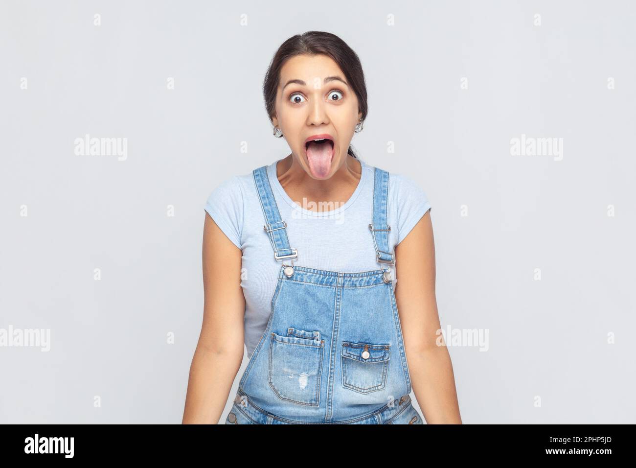 Portrait of disobedient crazy woman wearing denim overalls sticking out ...
