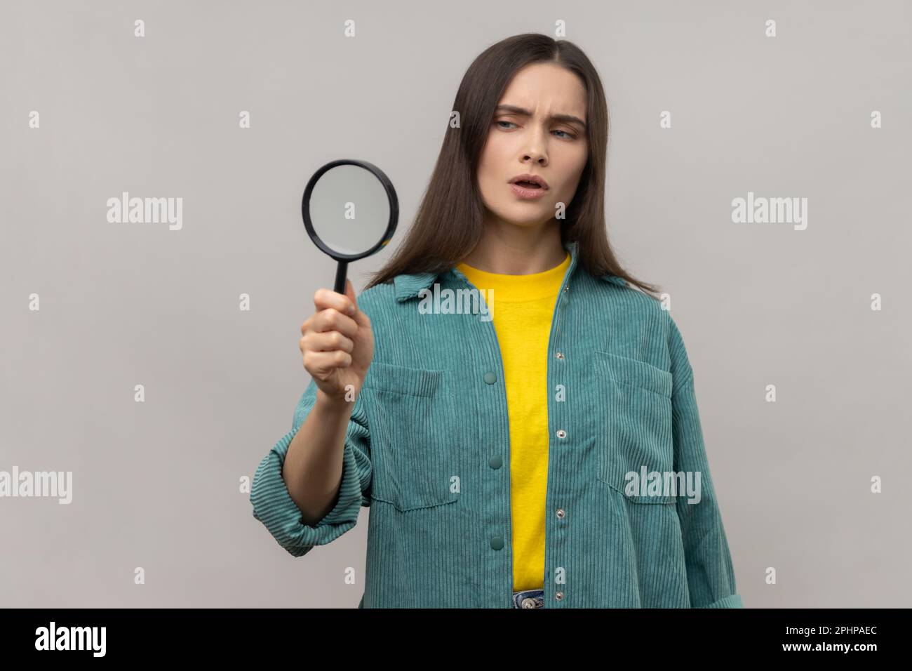 Curious woman with dark hair looking away through magnifying glass ...