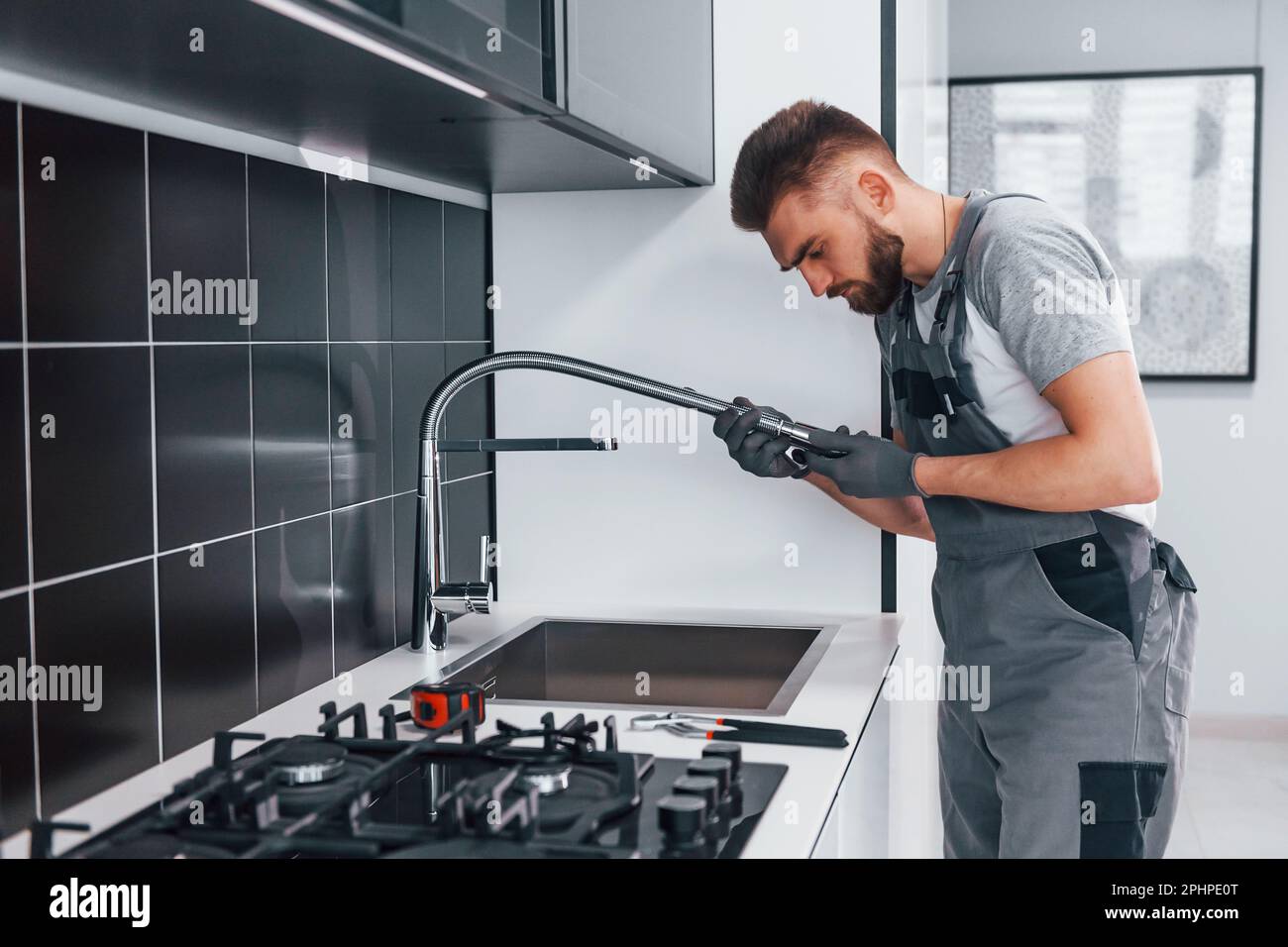 Young professional plumber in grey uniform fixing water tap on the ...