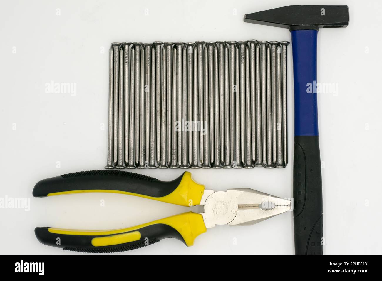 Metal nails, navy blue hammer, yellow pliers on a white background ...