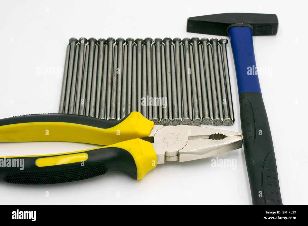 Metal nails, navy blue hammer, yellow pliers on a white background ...