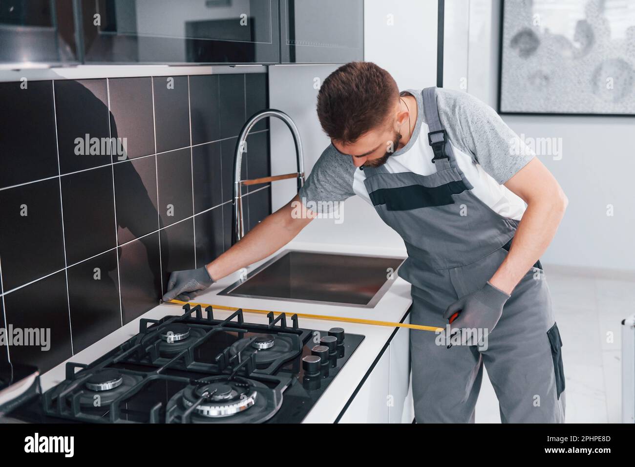 Young professional plumber in grey uniform measuring table by using ...
