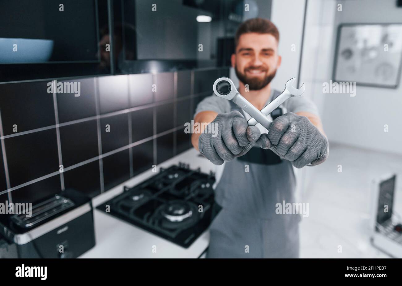 Young professional plumber in grey uniform standing on the kitchen and ...