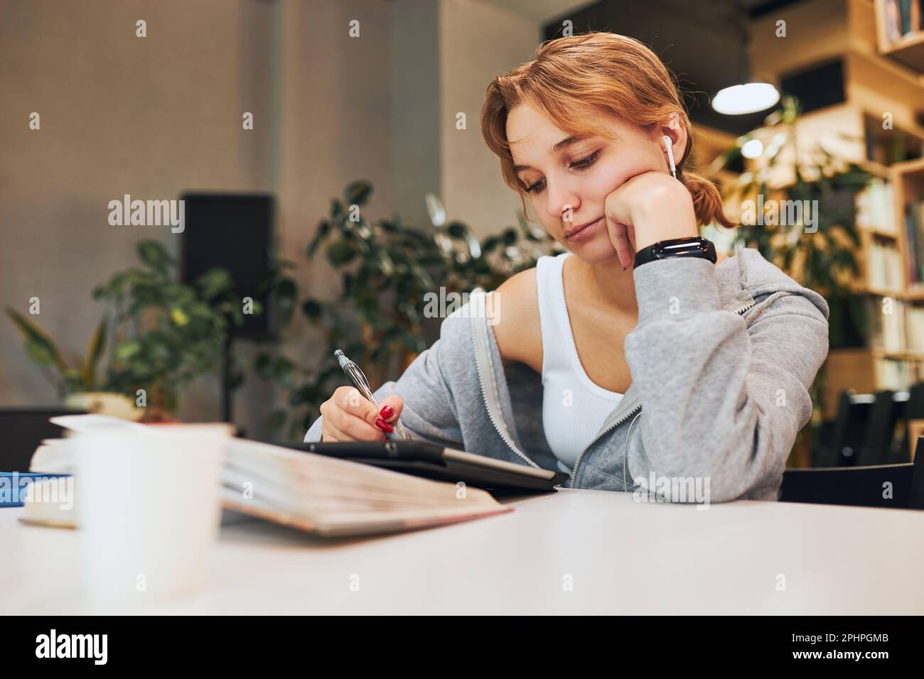 Student learning in university library. Young woman writing essay and ...