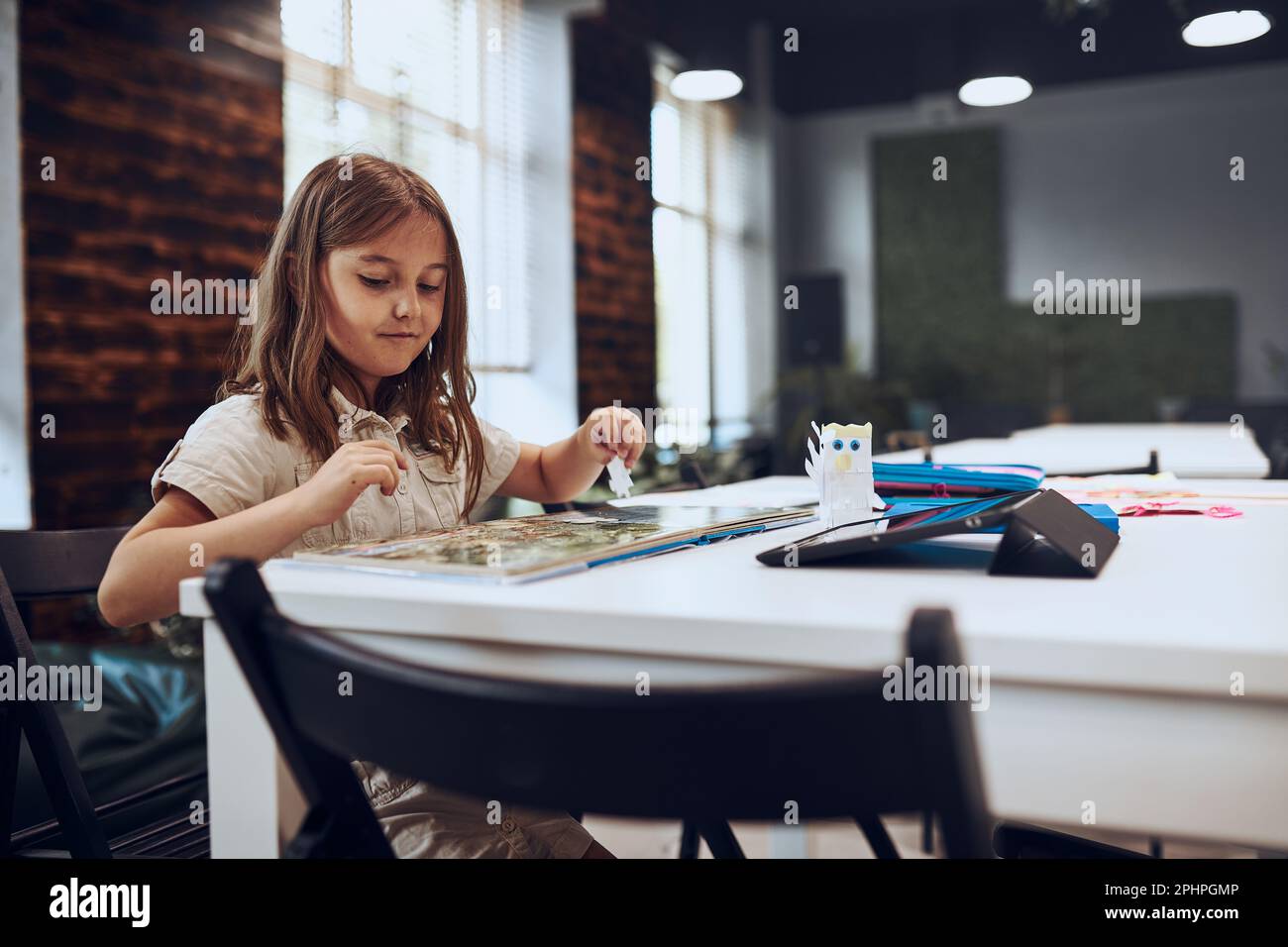 Schoolgirl doing puzzle and reading book in school library. Primary ...