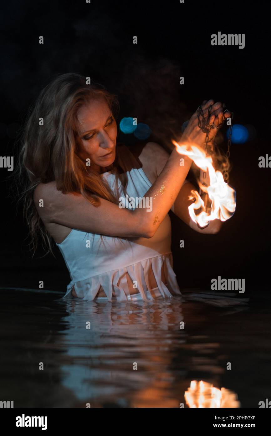 Caucasian woman dancing with fire in the water. Fire show at sea ...