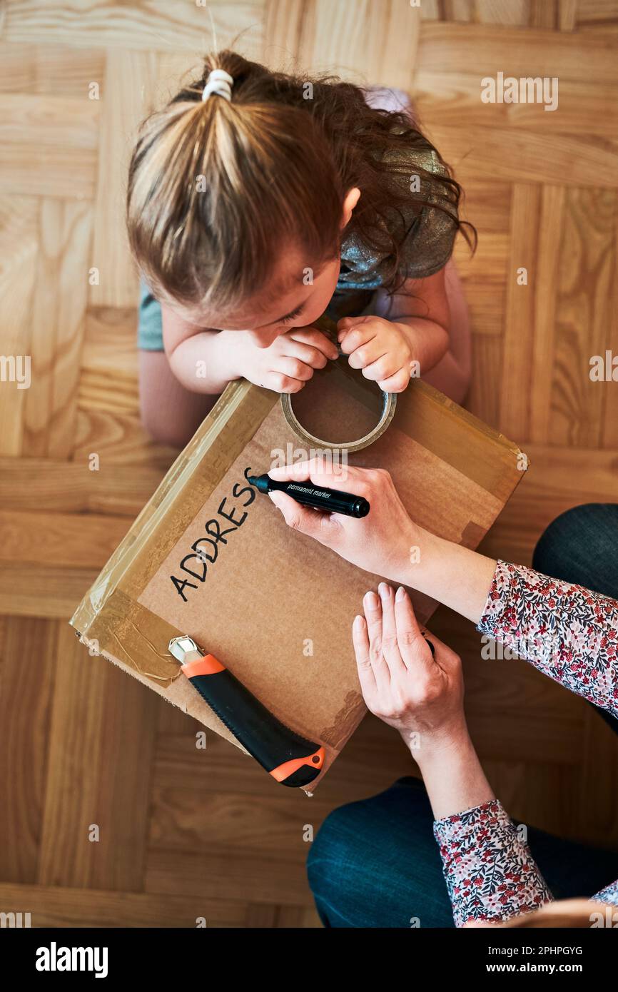 Woman writing an address on a cardboard box parcel in room at home ...
