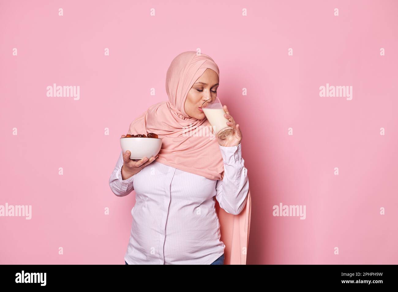 Lovely Muslim pregnant woman in pink hijab, holding a bow with dates ...